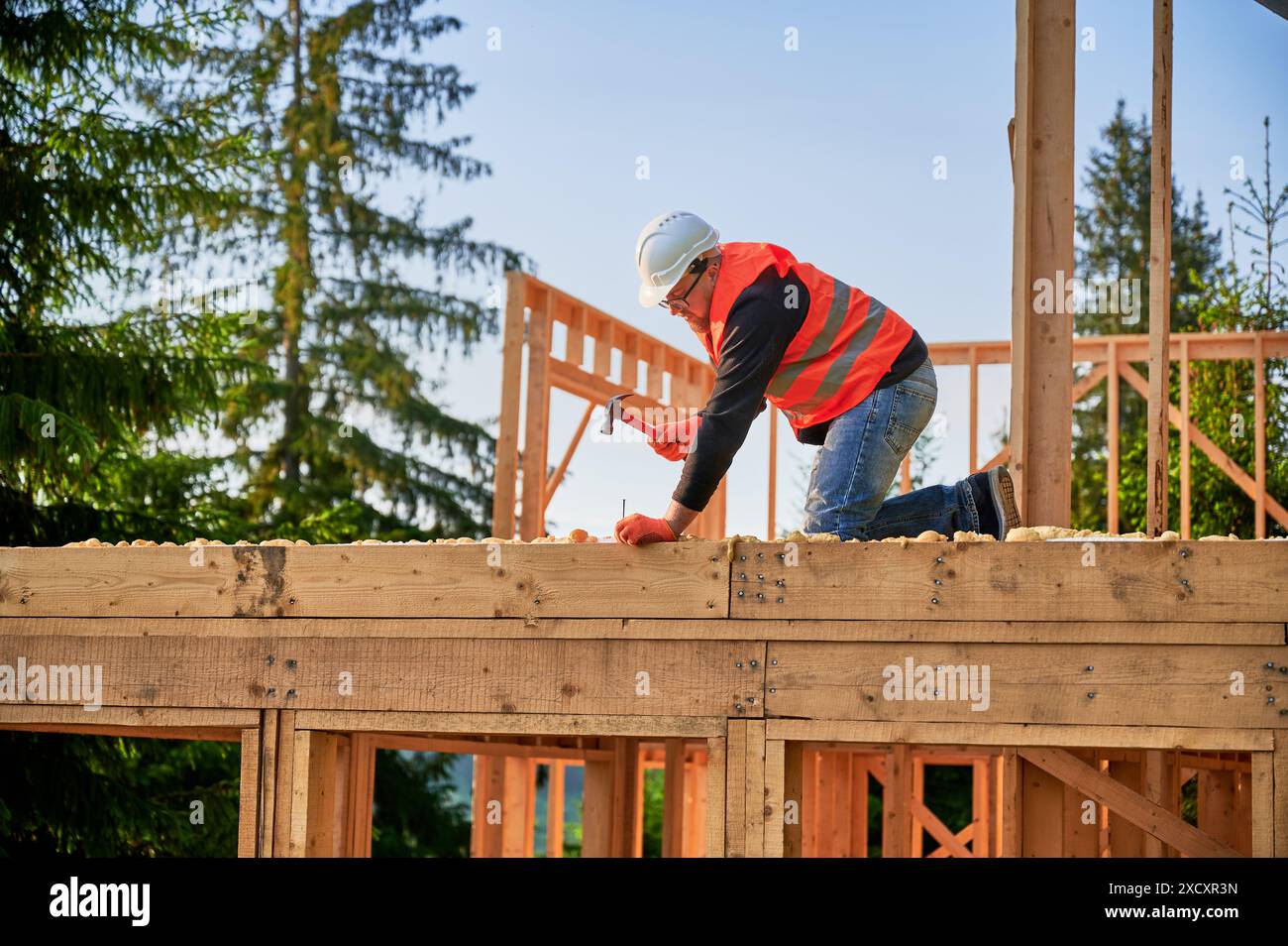 Carpenter constructing two-story wooden frame house near forest ...