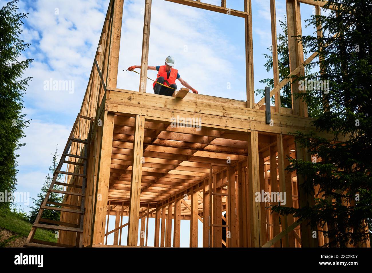 Carpenter constructing timber-framed two-story building. Man measures ...