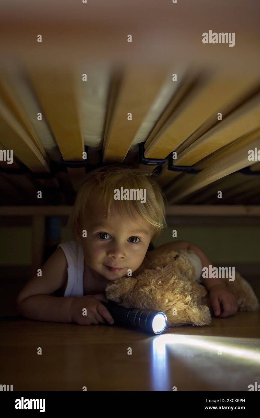 Little child, hiding under the bed, hugging teddy bear and holding ...
