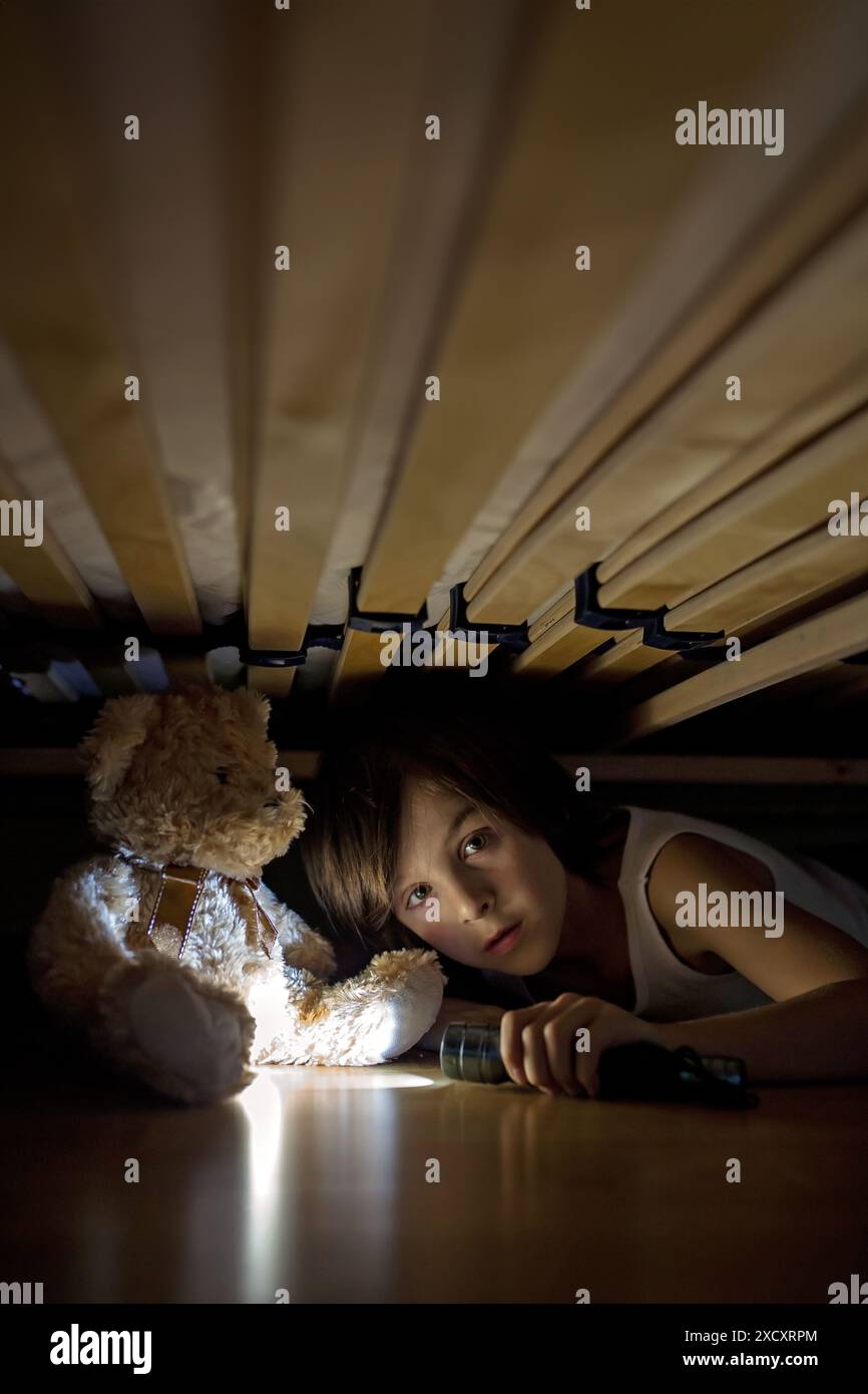 Little child, hiding under the bed, hugging teddy bear and holding ...