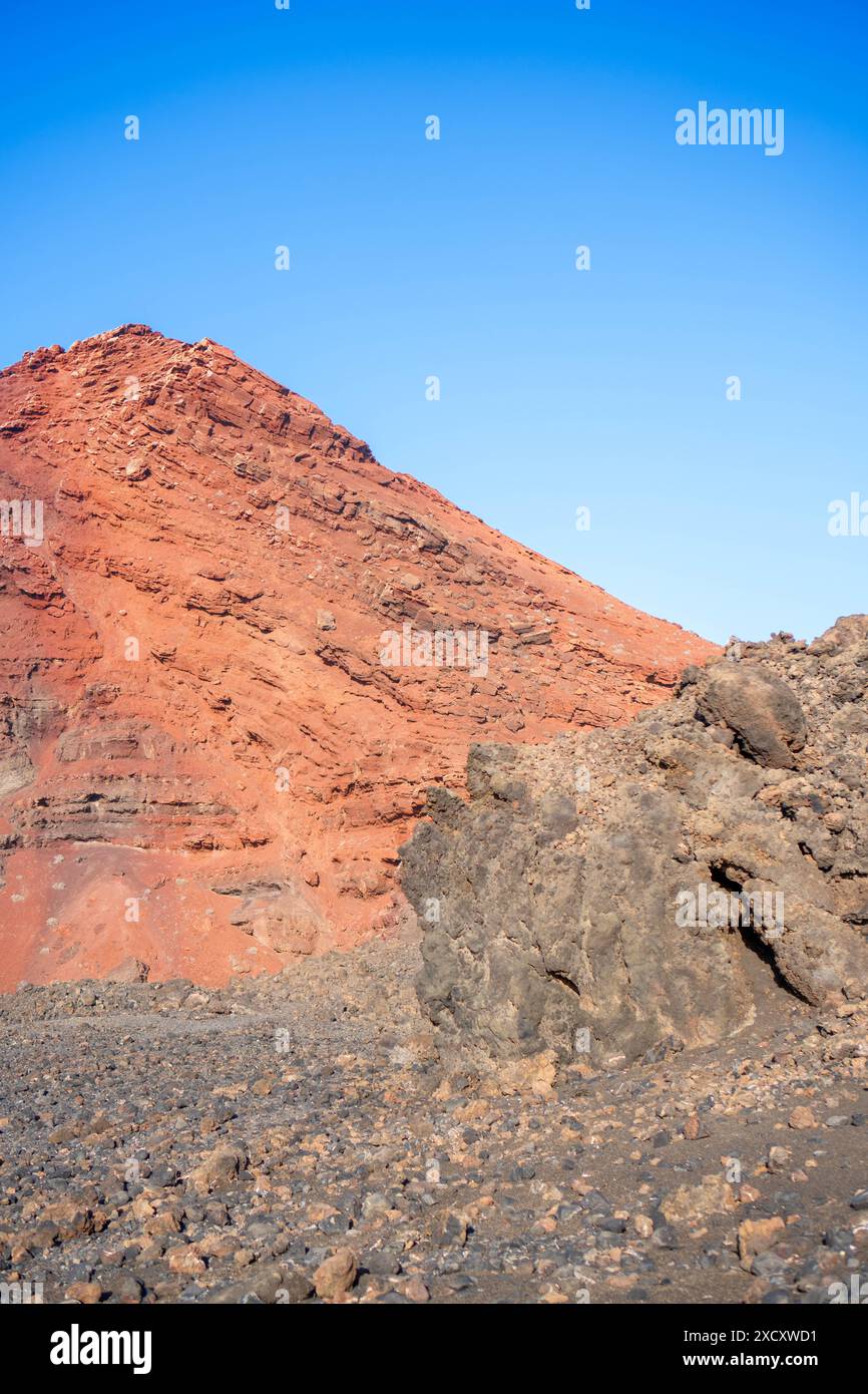 A red volcanic mountain rises against a clear blue sky, the foreground ...