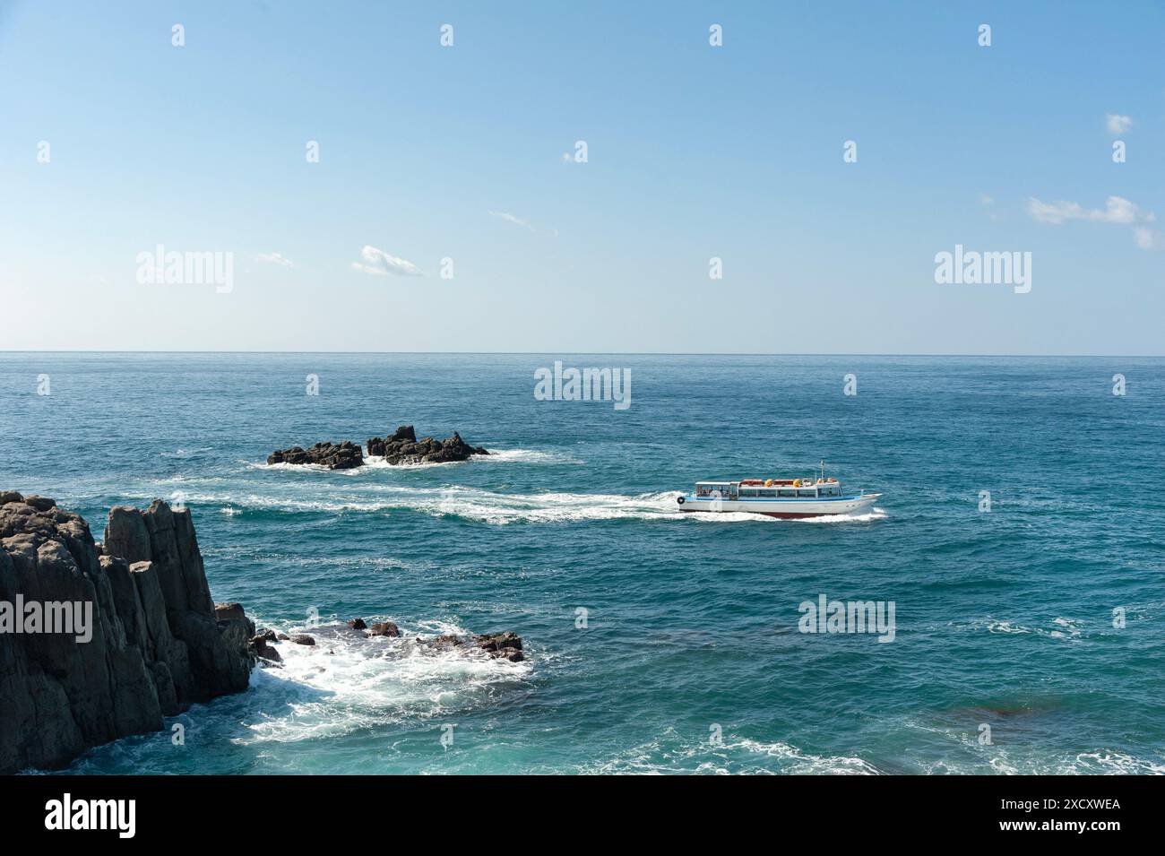 A tour boat sailing near the cliffs of Tojinbo along the coastline of ...