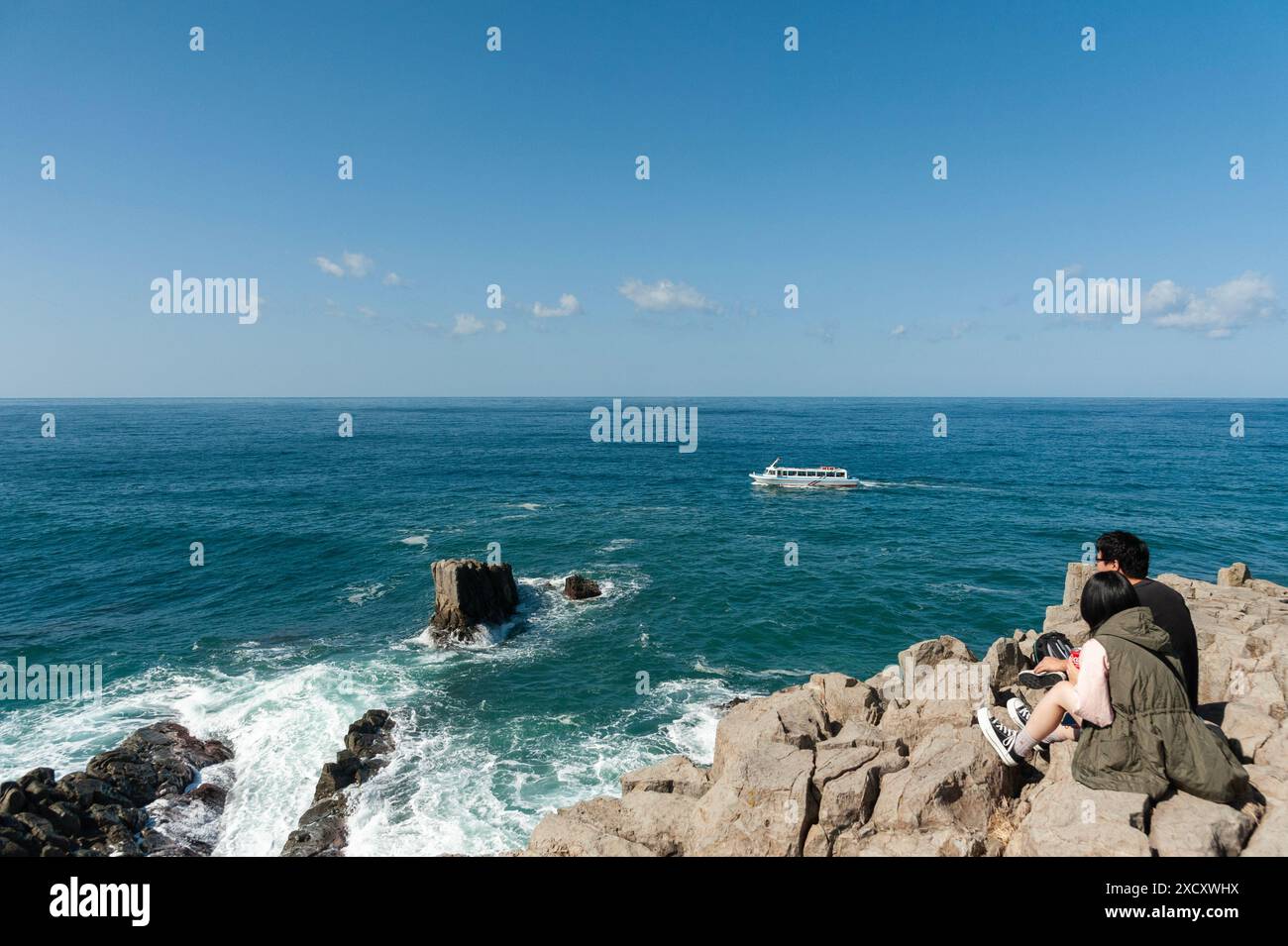 Tourists watch a tour boat sail pass the cliffs at Tojinbo in the Sea ...