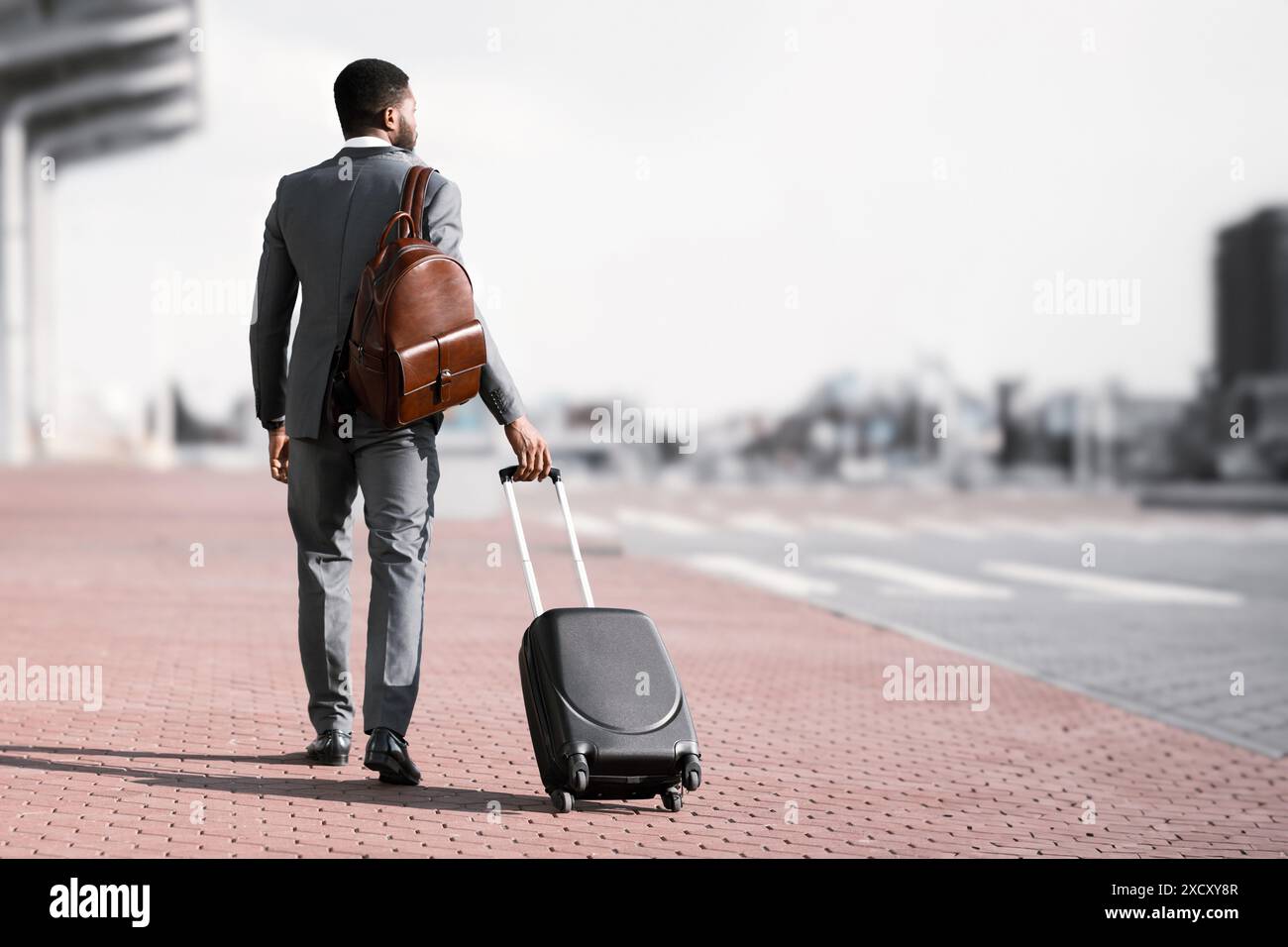 Back view of businessman walking with luggage outside modern building ...