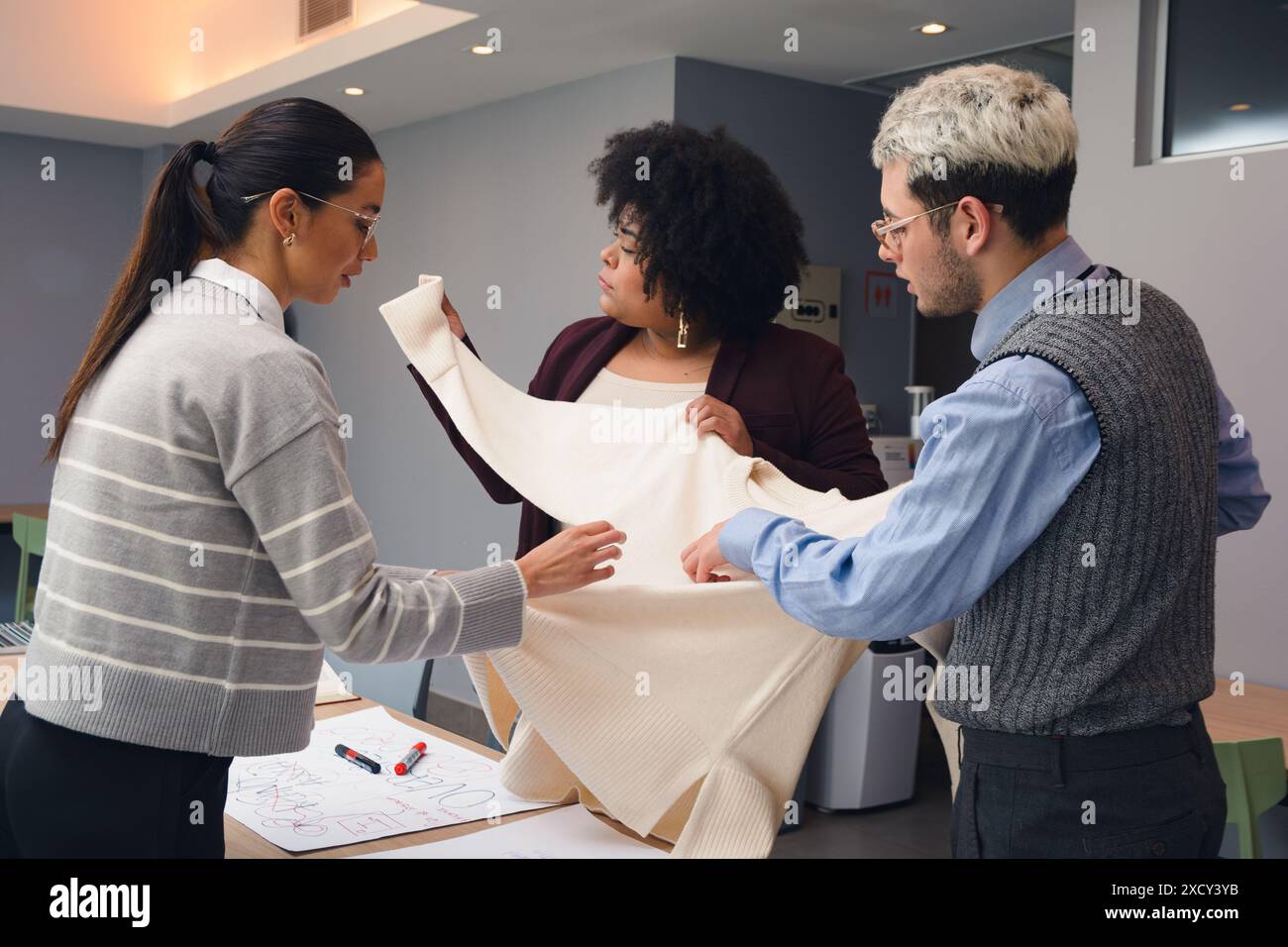 Two Women and a Man, are standing around a table, one of them holding ...