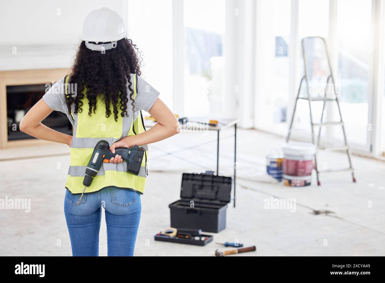 Construction site, drill and back of woman with tools, helmet and thinking for project. Female ...