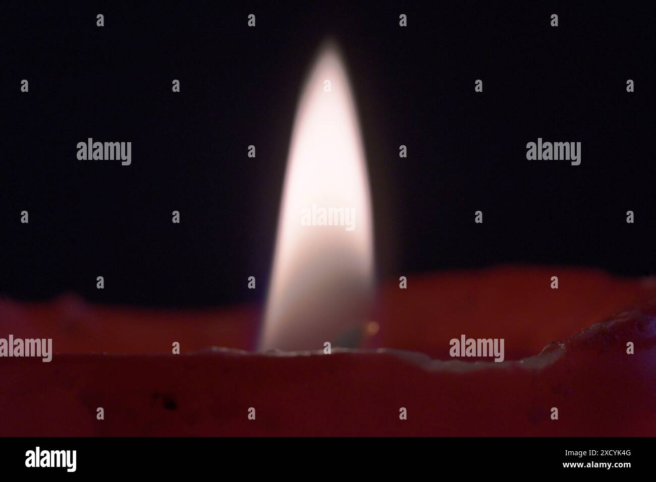 Flame of a burning red wax candle with black horizontal background ...