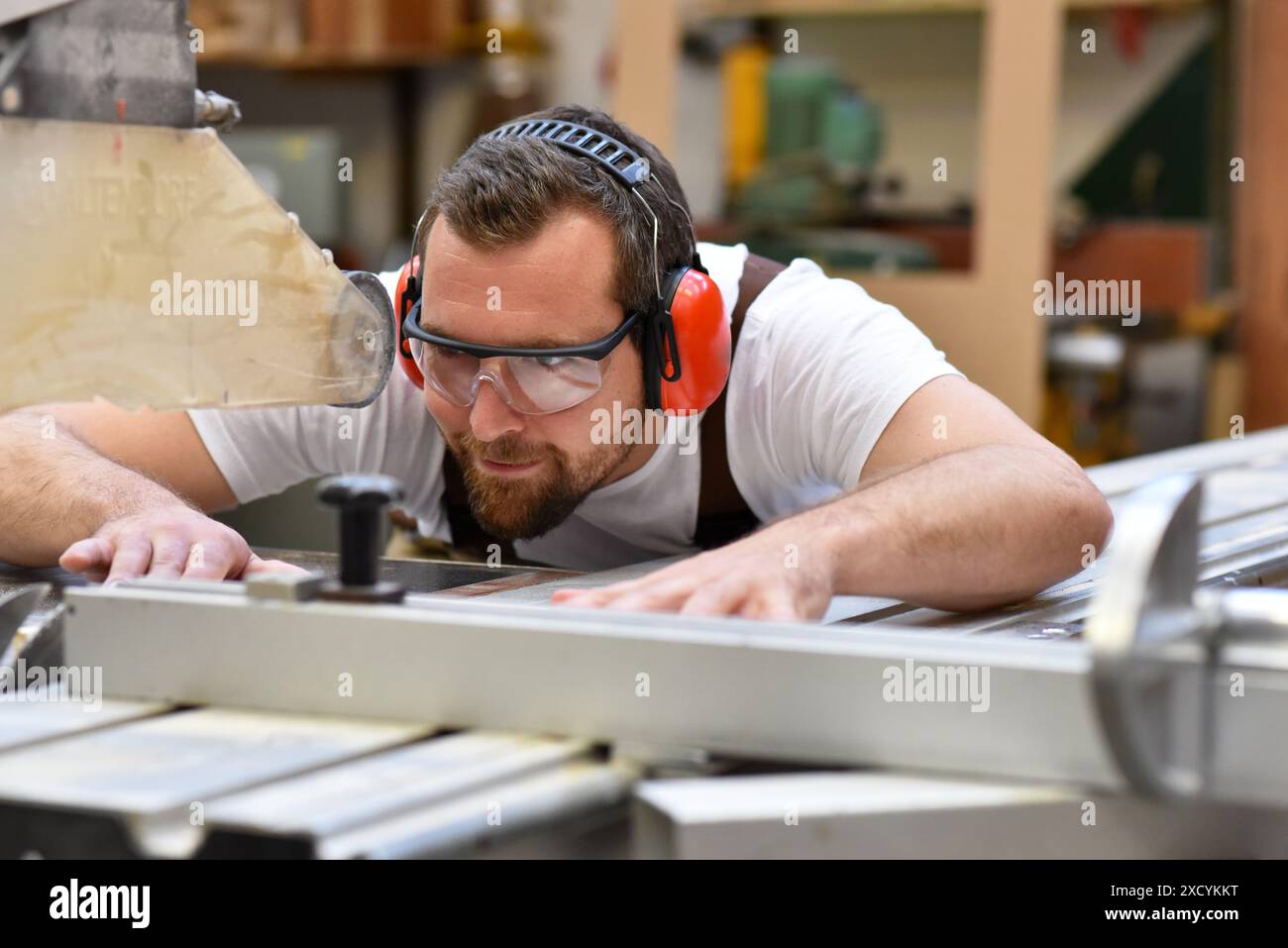 young carpenter in working clothes works in the joinery on a sanding ...