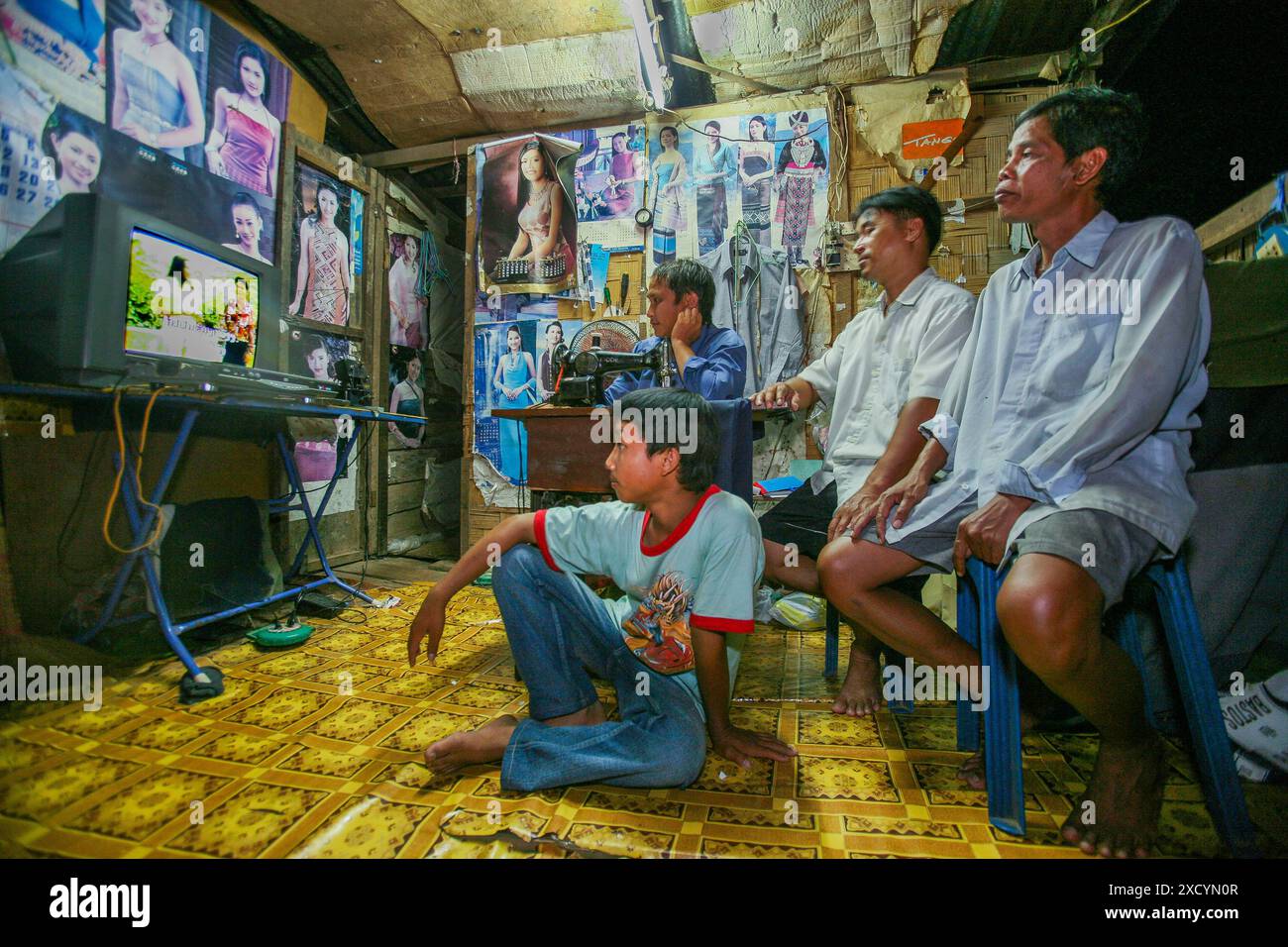 Laos, Vientiane. Tailors watching television in their small hut near ...