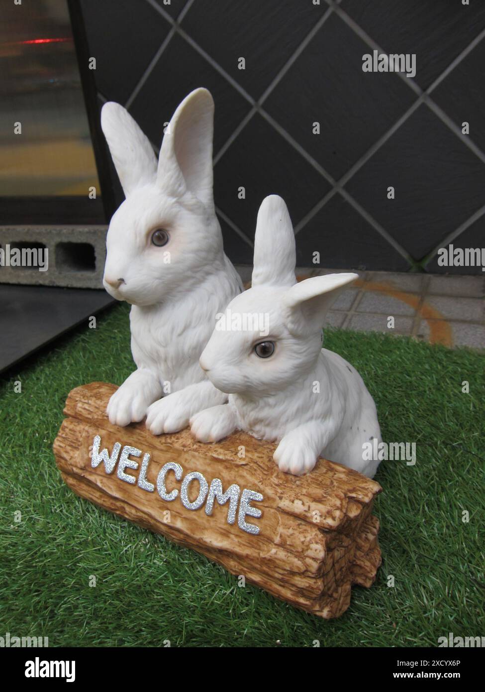 A decorative welcome sign with two white rabbit figurines on artificial ...