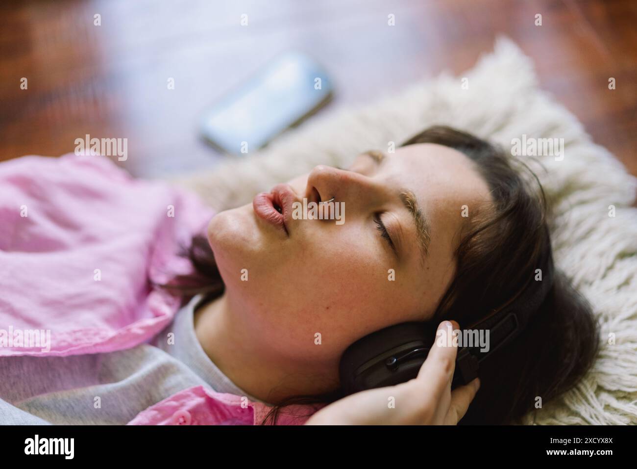 A teengirl is lying on her back on a wooden floor, wearing headphones ...
