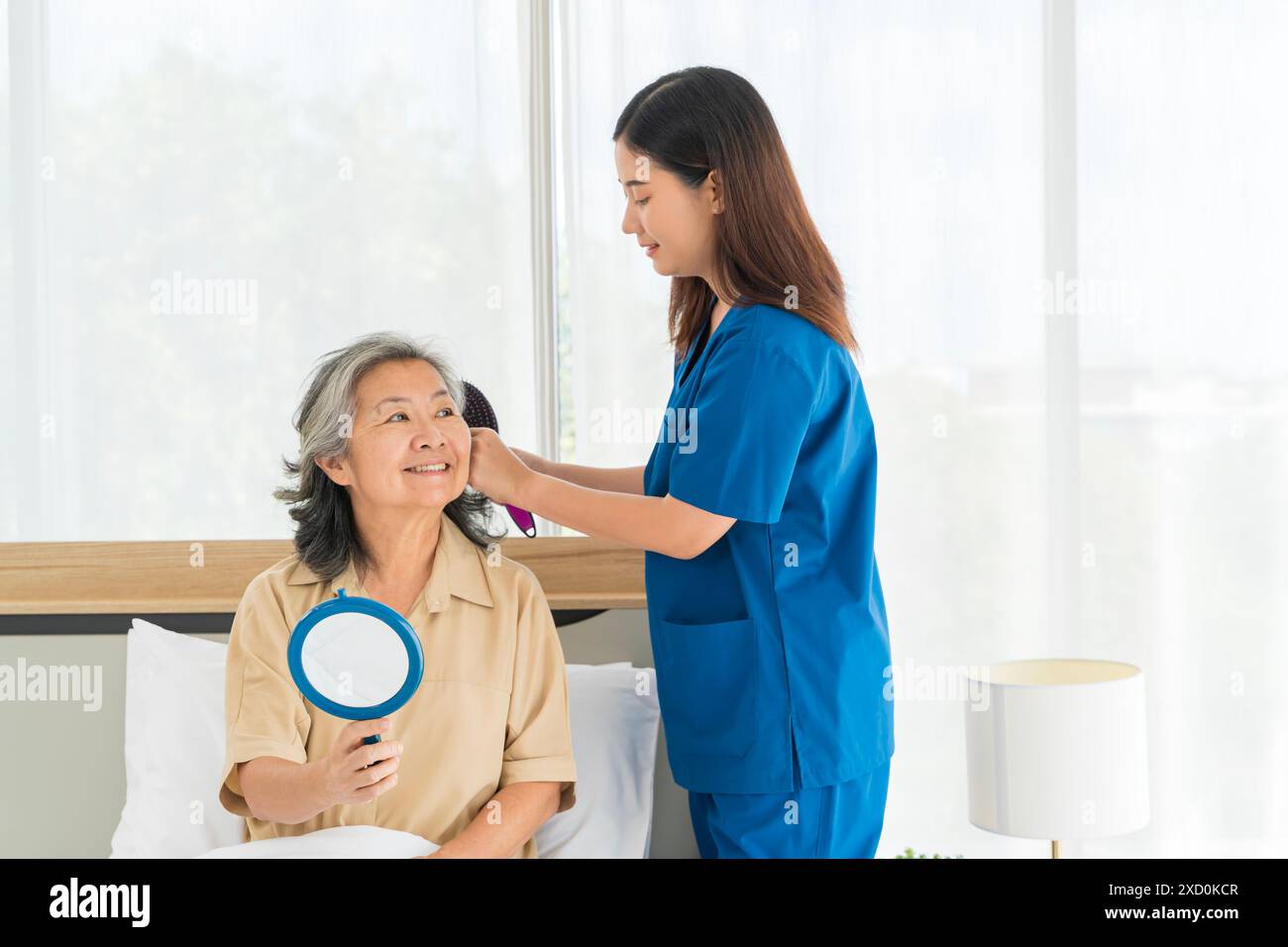 A woman in a blue uniform is helping an older woman with her hair ...