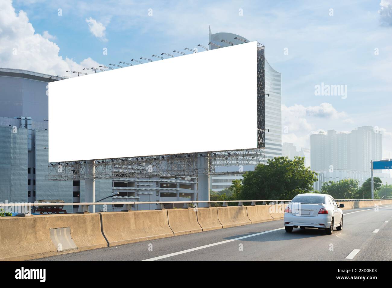 A white car is driving down a highway next to a large billboard. The ...