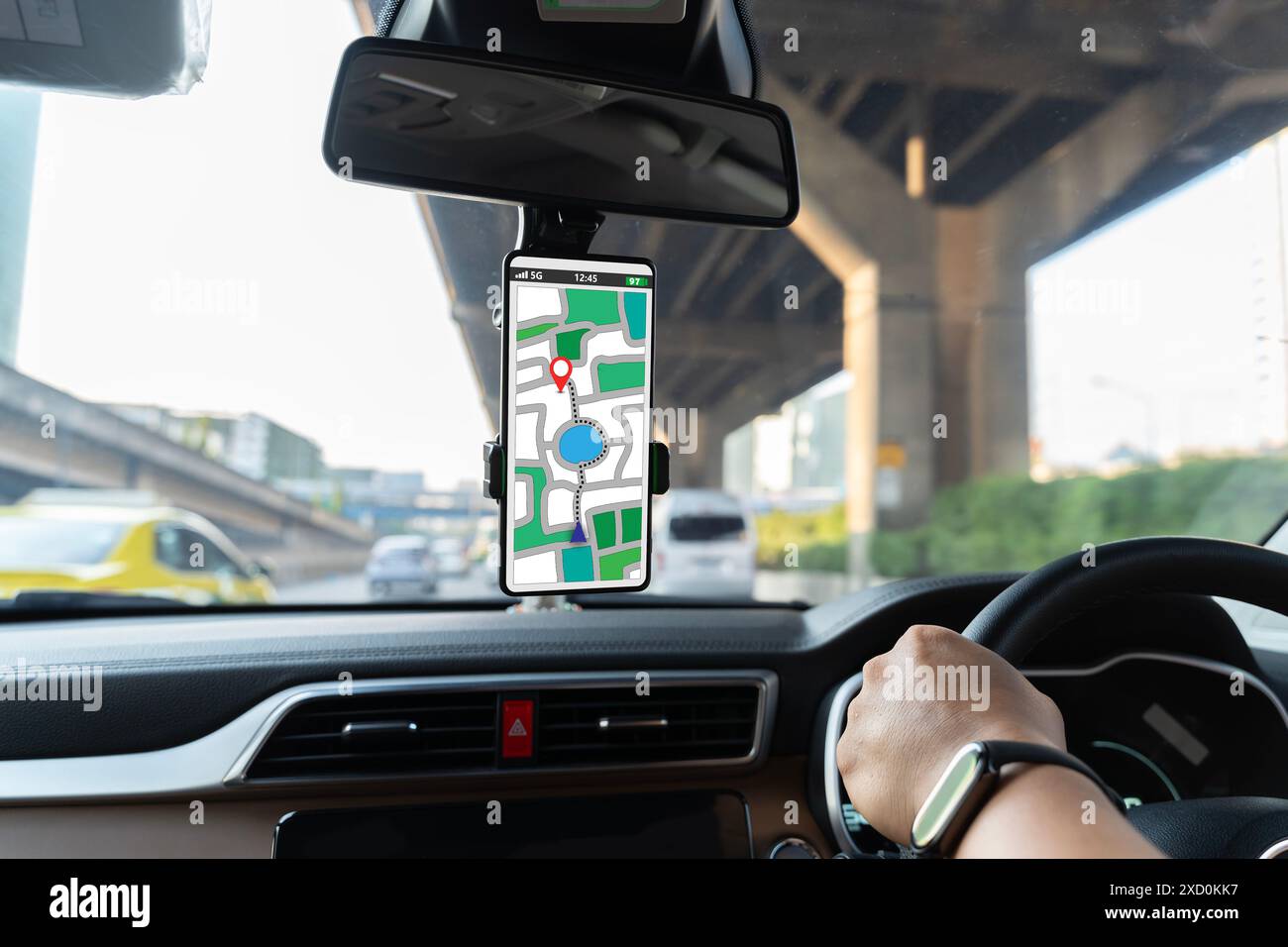 A person is driving a car with a phone mounted on the dashboard. The phone is displaying a map ...