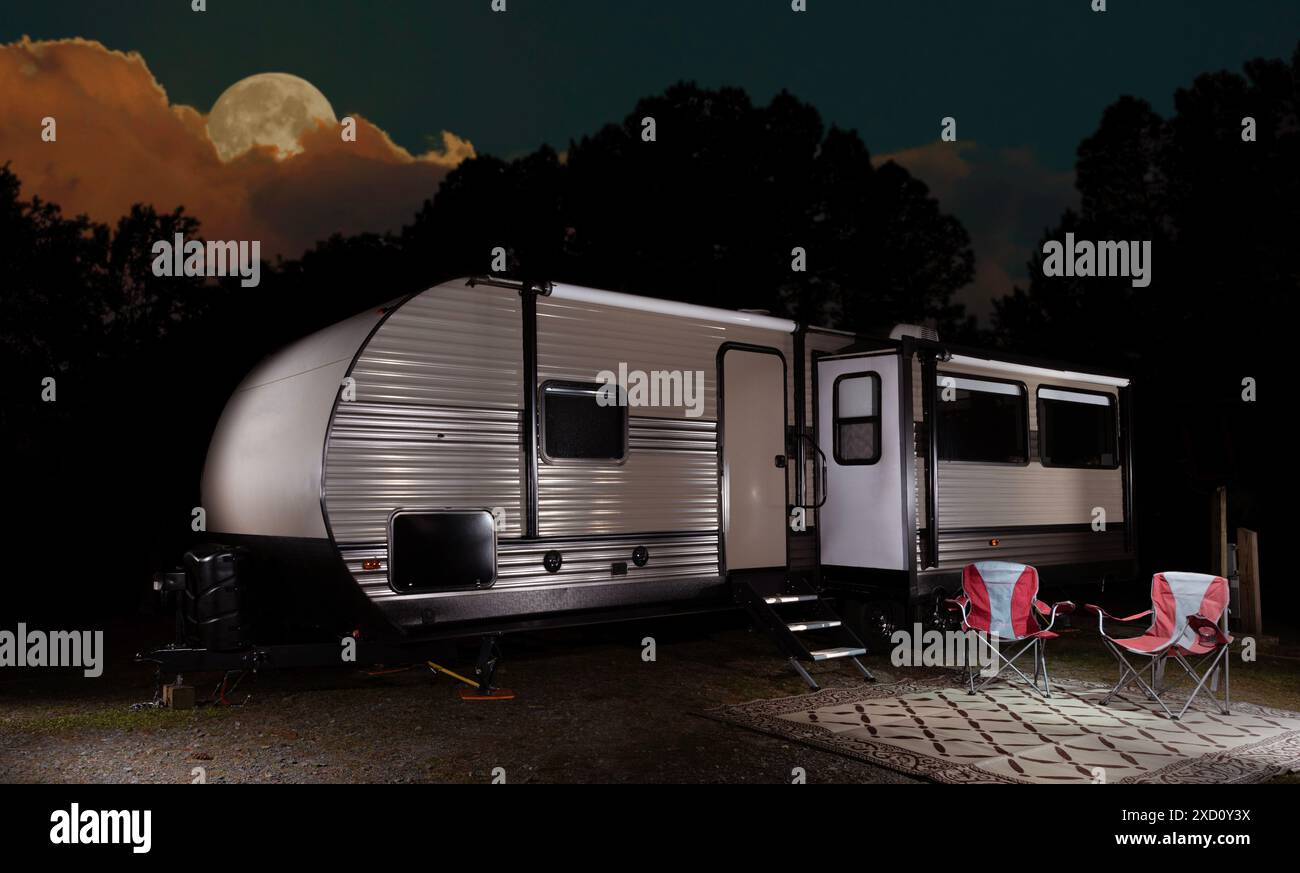 Yellow and orange moon rising behind a camper trailer all set up for ...