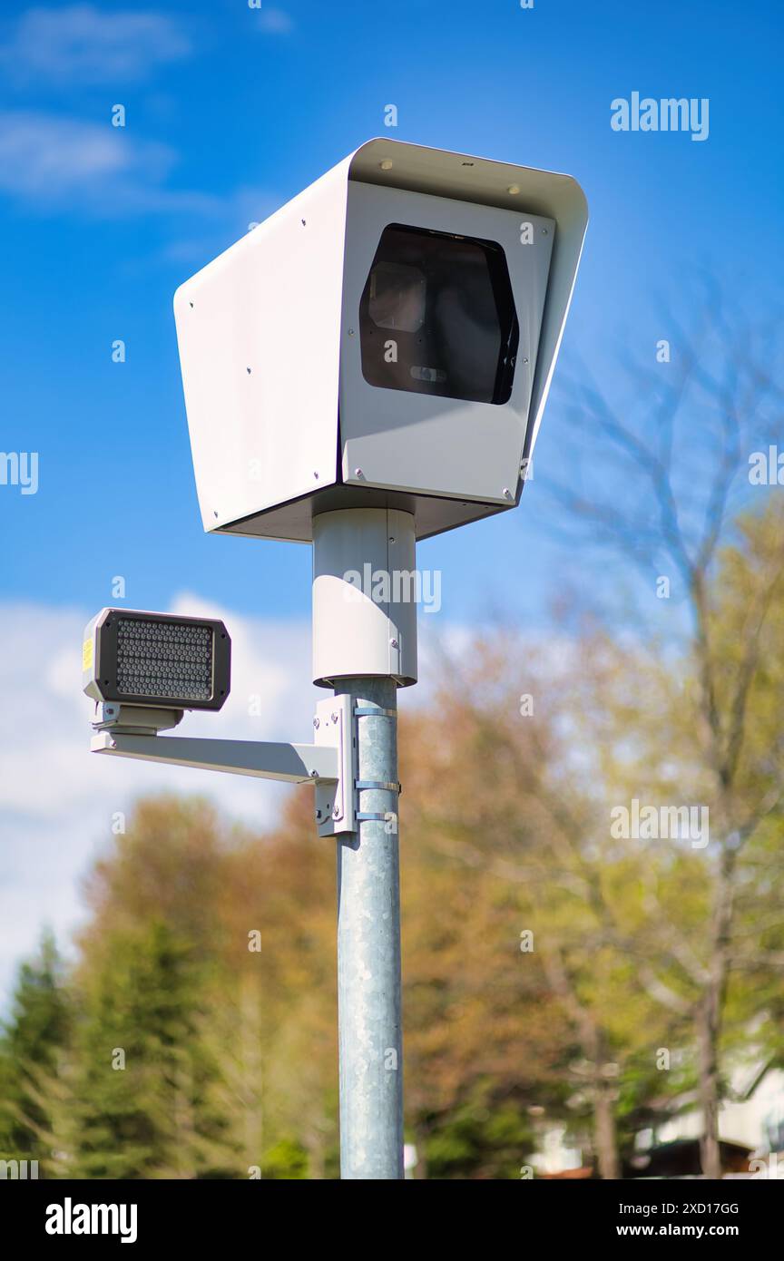 A speed camera system mounted on a grey metal pole against a clear blue ...