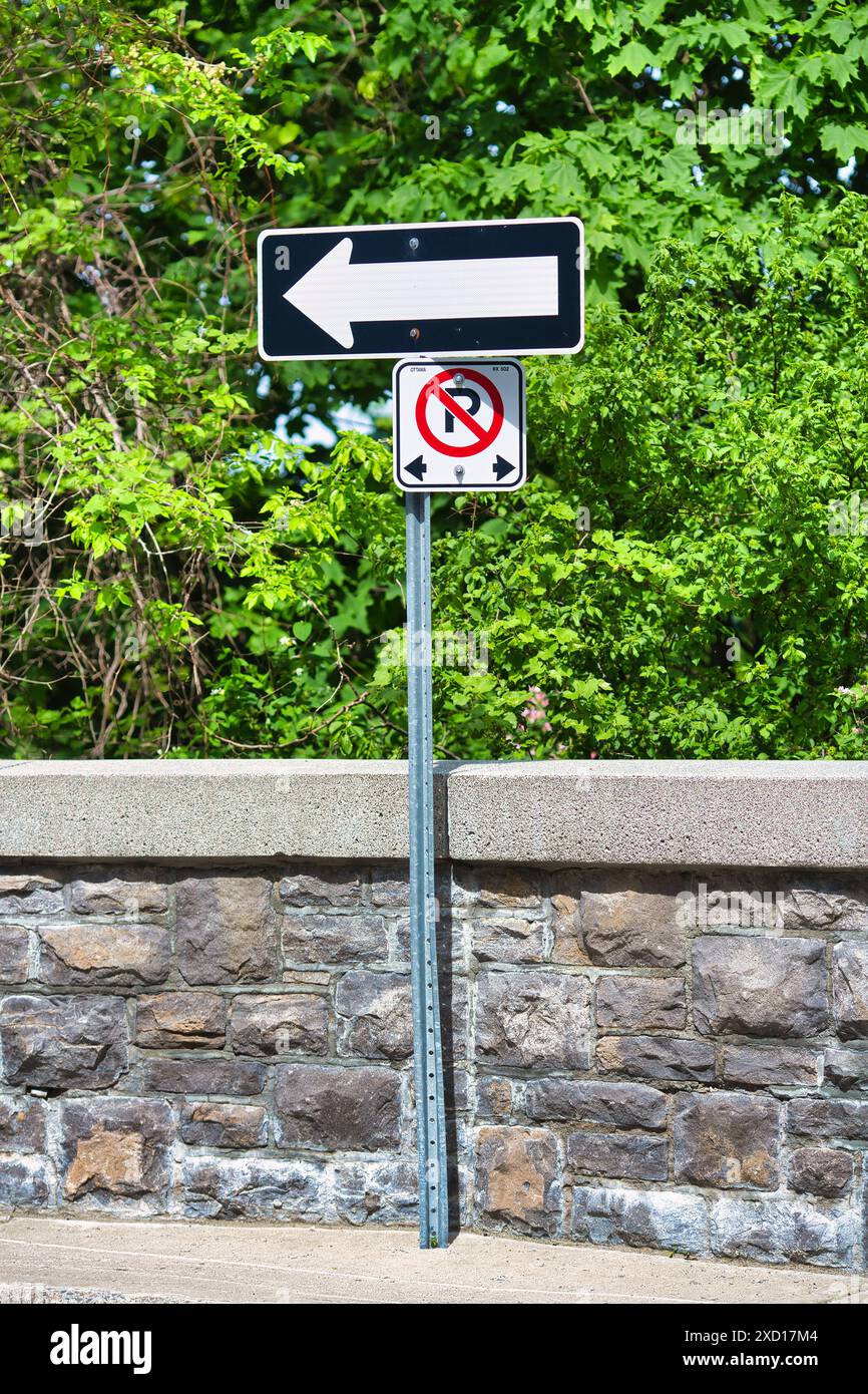 A metal pole supporting two road signs against a background of green ...