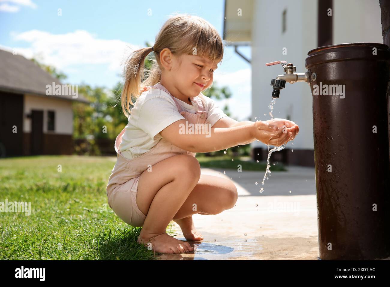 Water scarcity. Cute little girl drawing water with hands from tap ...