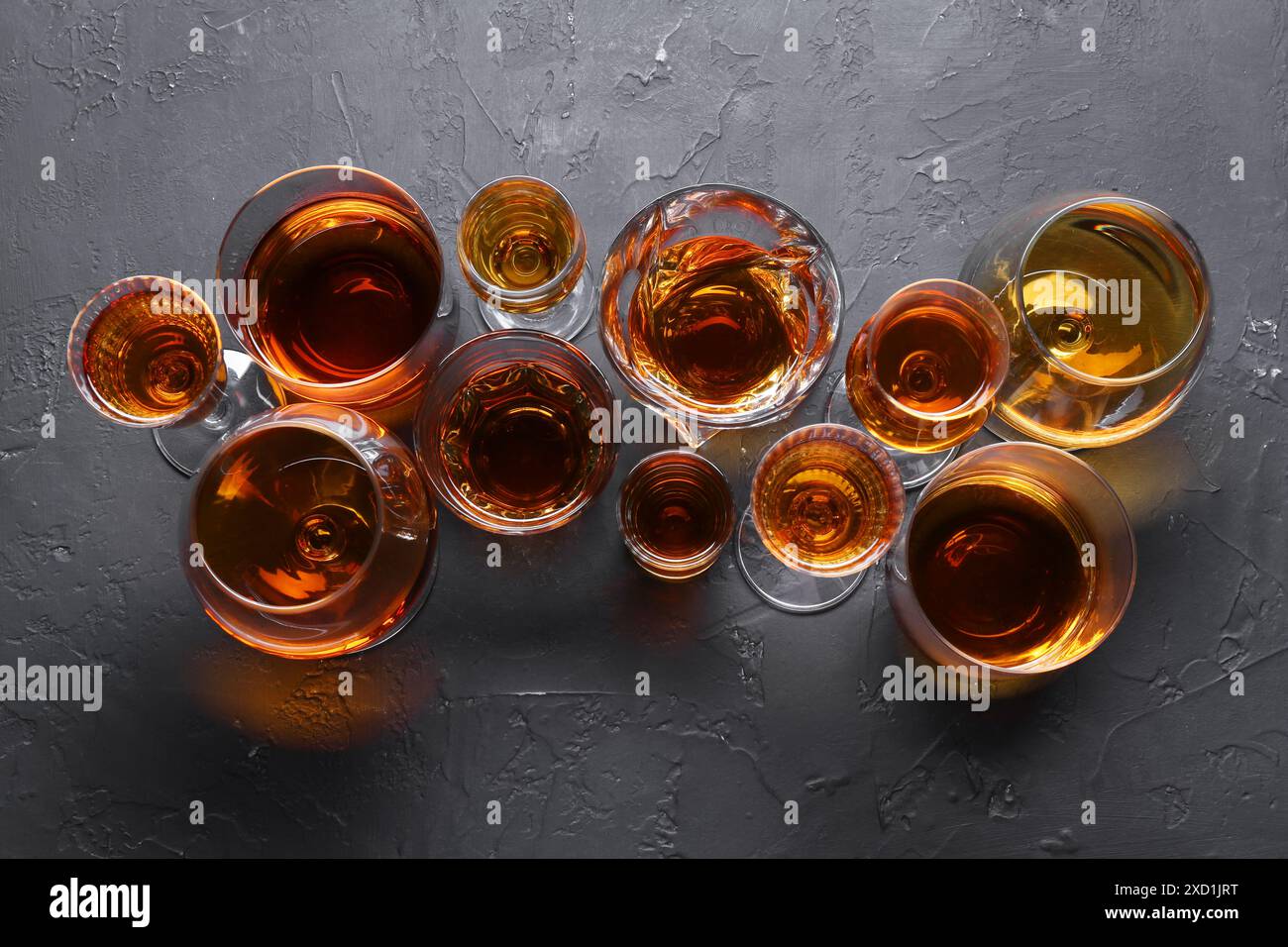 Many different liqueurs in glasses on dark textured table, flat lay ...