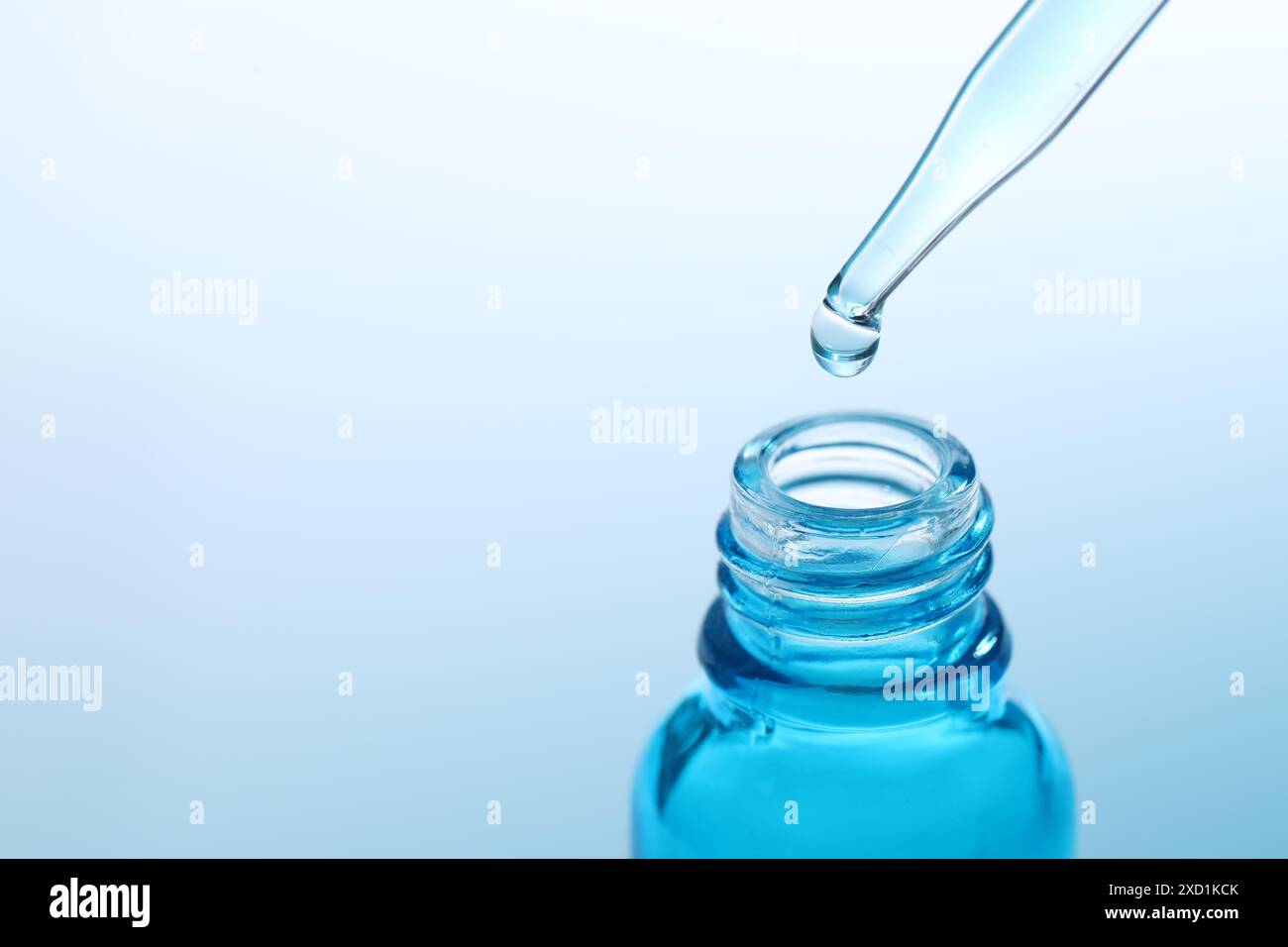 Dripping liquid from pipette into glass bottle on light blue background ...