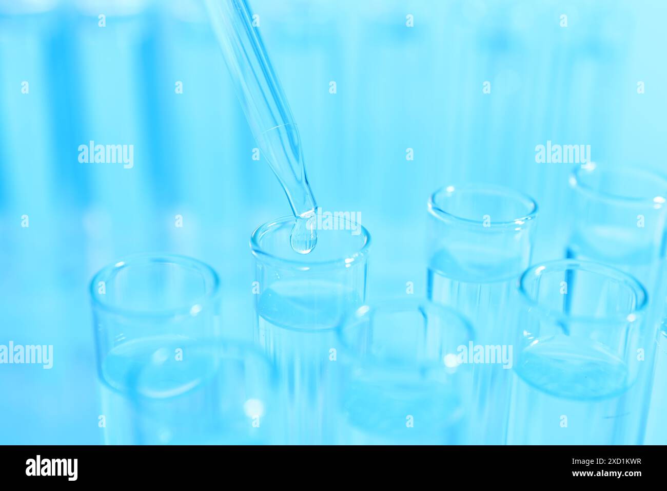 Dripping liquid from pipette into test tube on light blue background ...