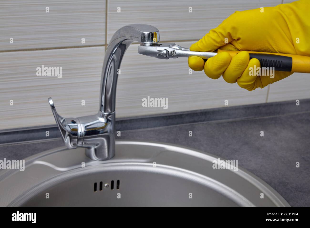 A plumber in yellow rubber gloves unscrews the faucet aerator with an ...