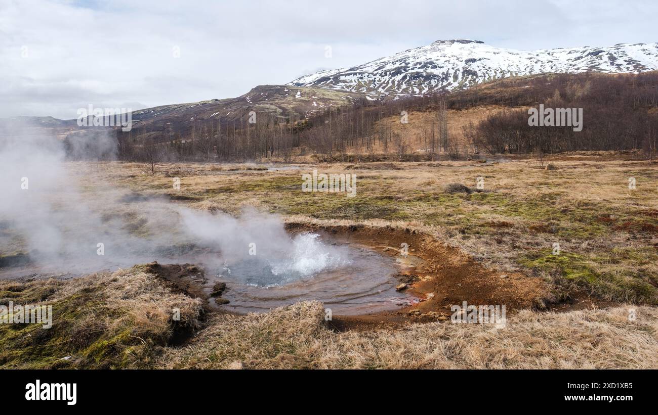 A steaming hot spring in a scenic Icelandic landscape with snow-capped ...