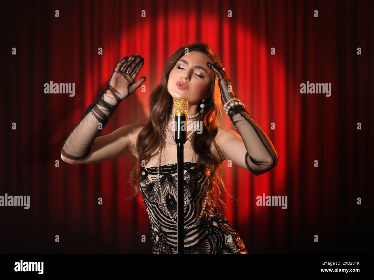 Beautiful singer performing in spotlight on stage against red curtain ...