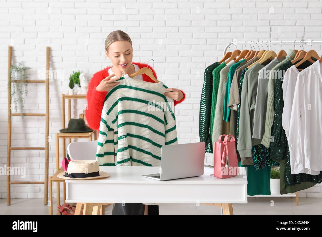 Female stylist with laptop and clothes on rack video chatting in studio ...