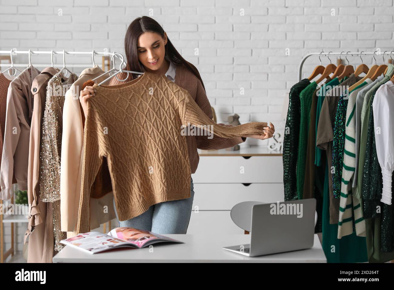 Happy female stylist with laptop and clothes on rack in studio Stock ...