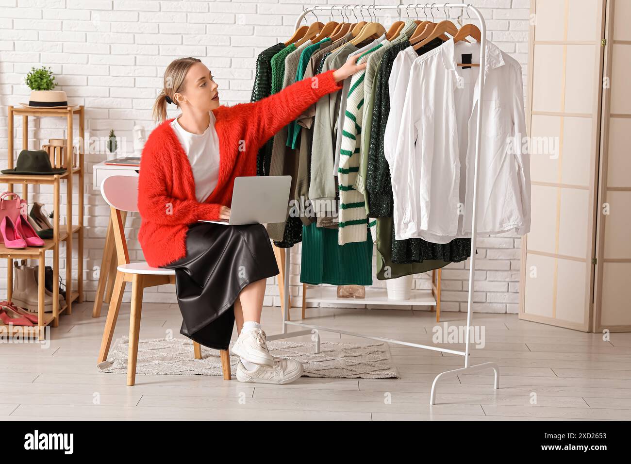 Female stylist with laptop and clothes on rack sitting in studio Stock ...