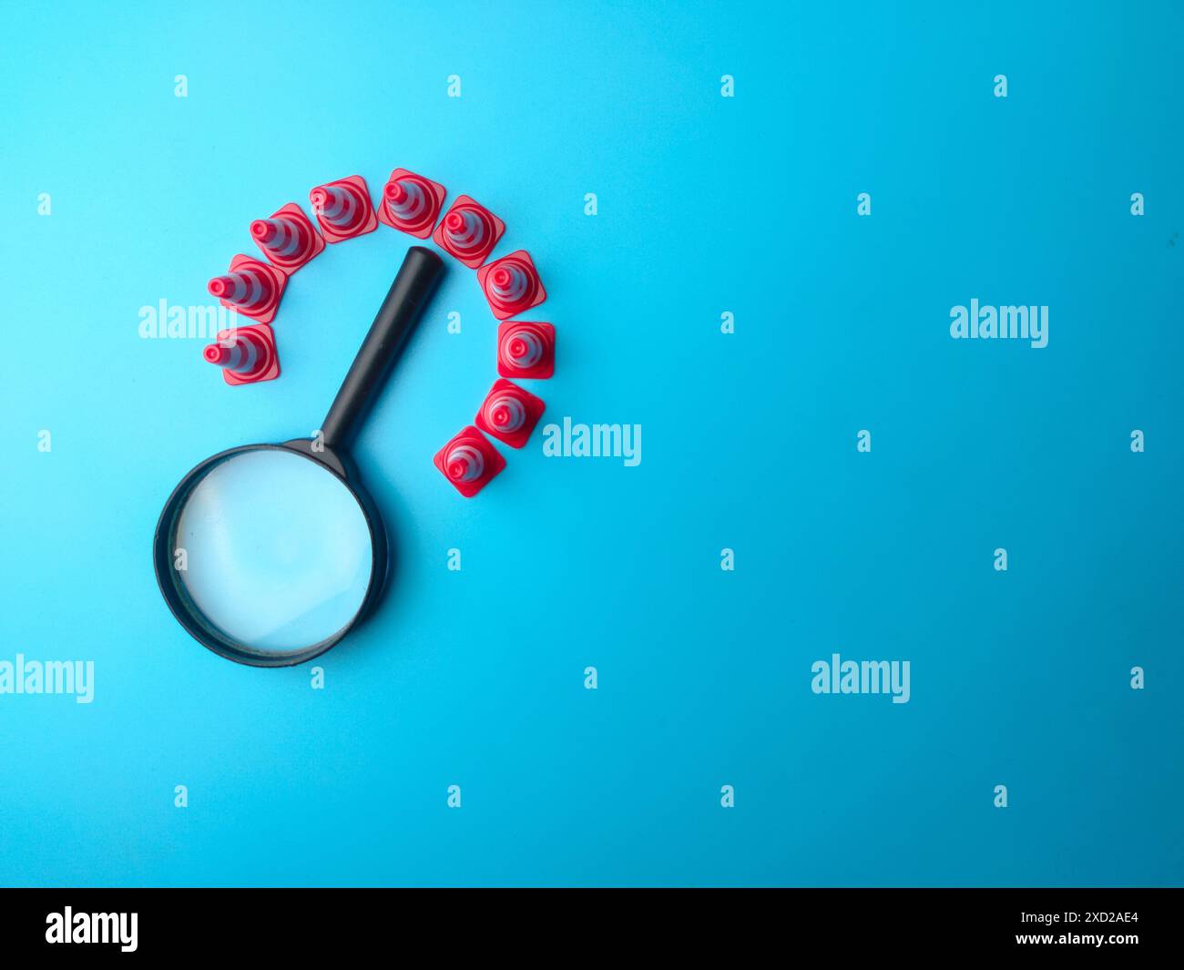 Mini plastic cones and magnifying glass on a blue background with copy ...