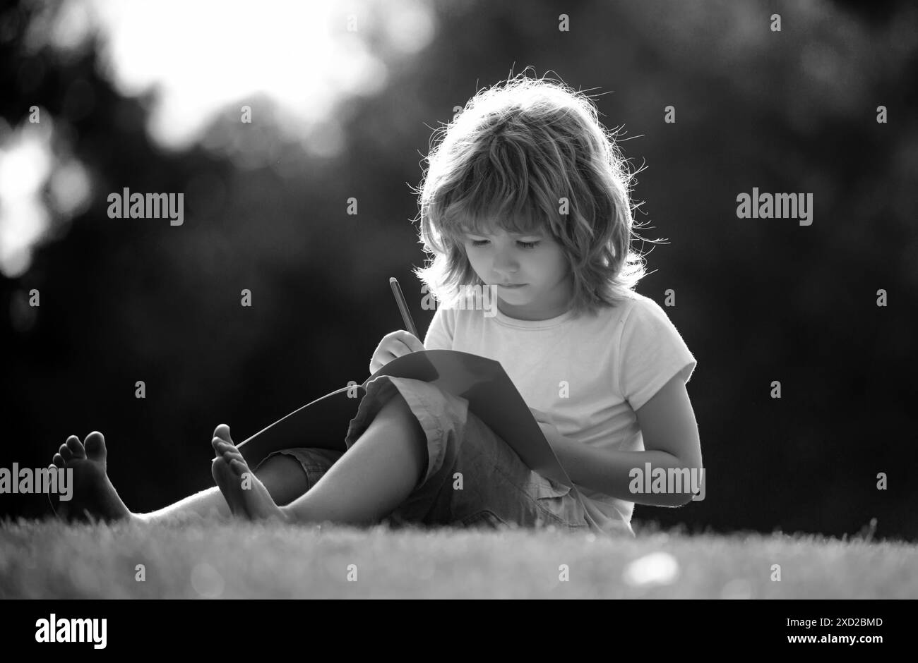 Funny child boy doing homework writing and reading in park on grass ...