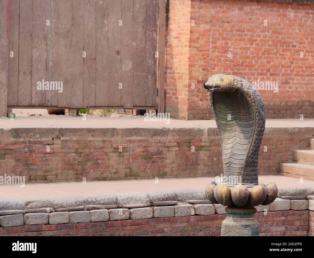 A close-up of a snake statue in front of a rustic brick wall and wooden ...