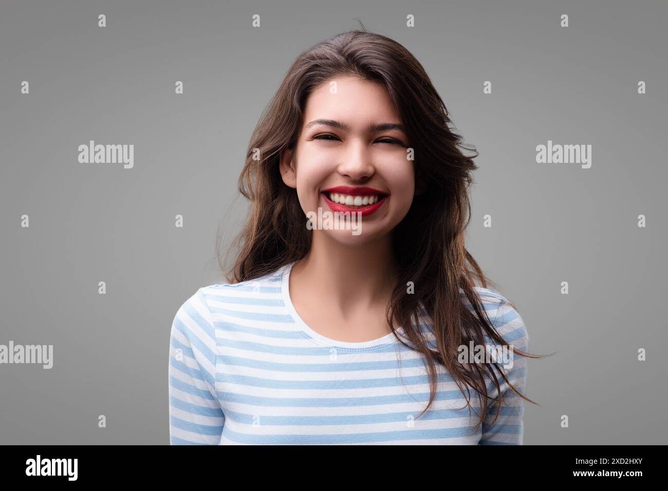 Young woman with long brown hair and a striped shirt smiles playfully ...