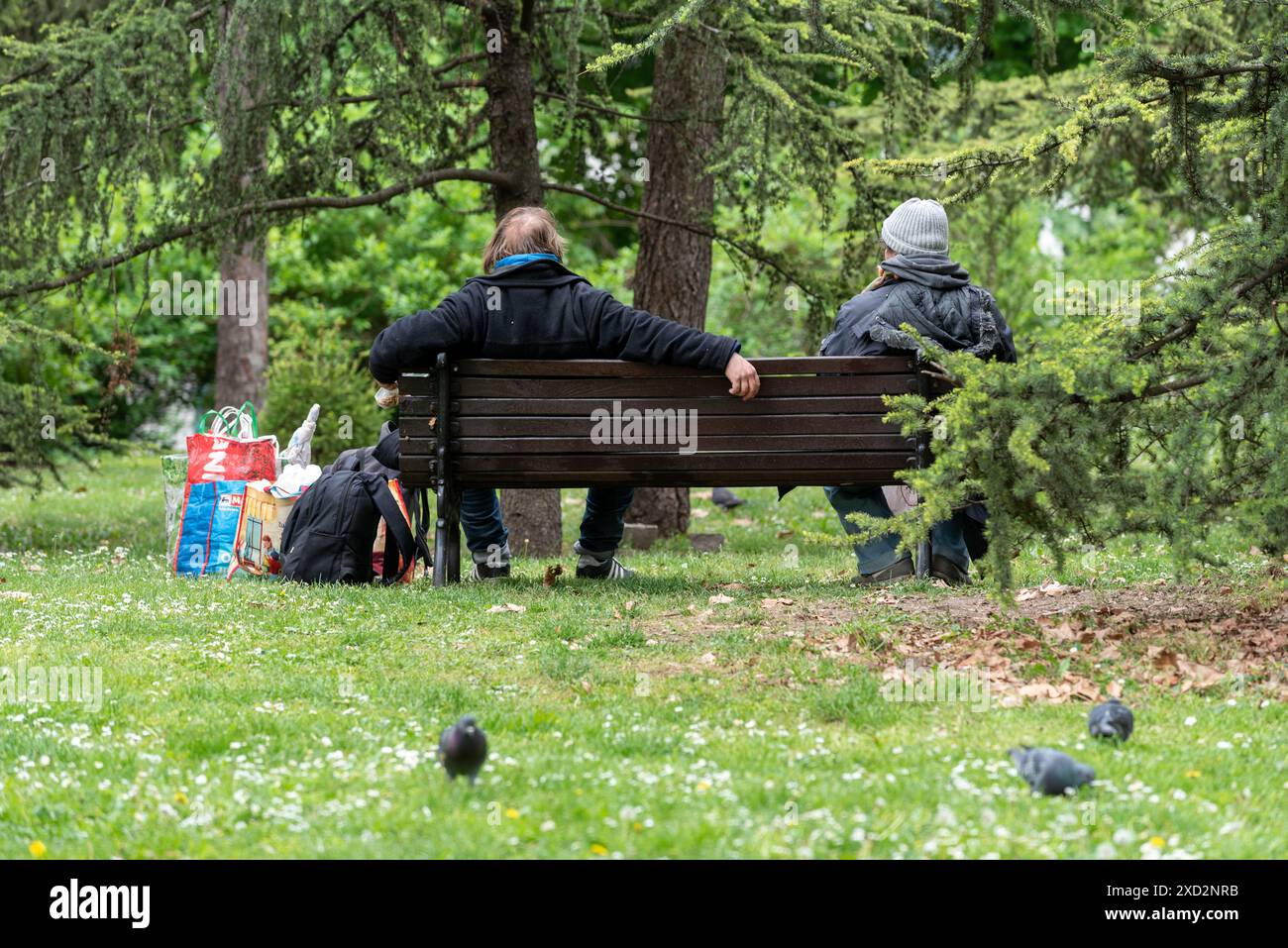 Pair of homeless people with their belongings, sat on a park bench ...