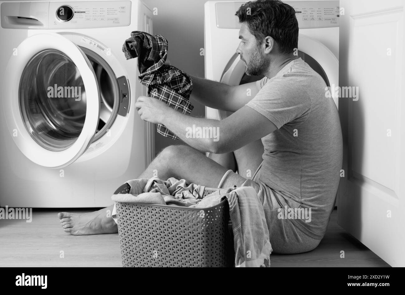 Man with clothes near washing machine. Handsome man sits in front of ...