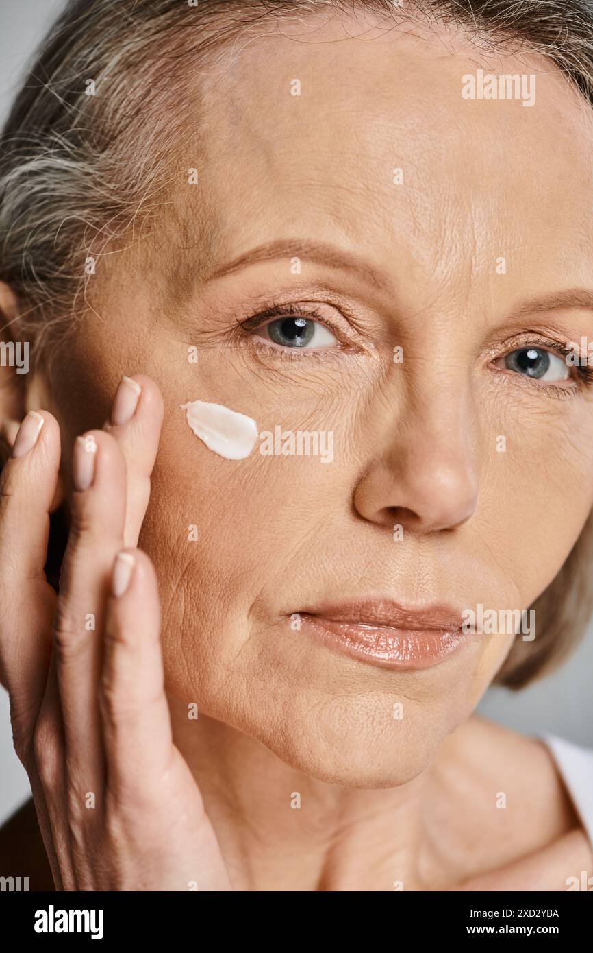 An elegant older woman gently applying cream to her face, taking care ...