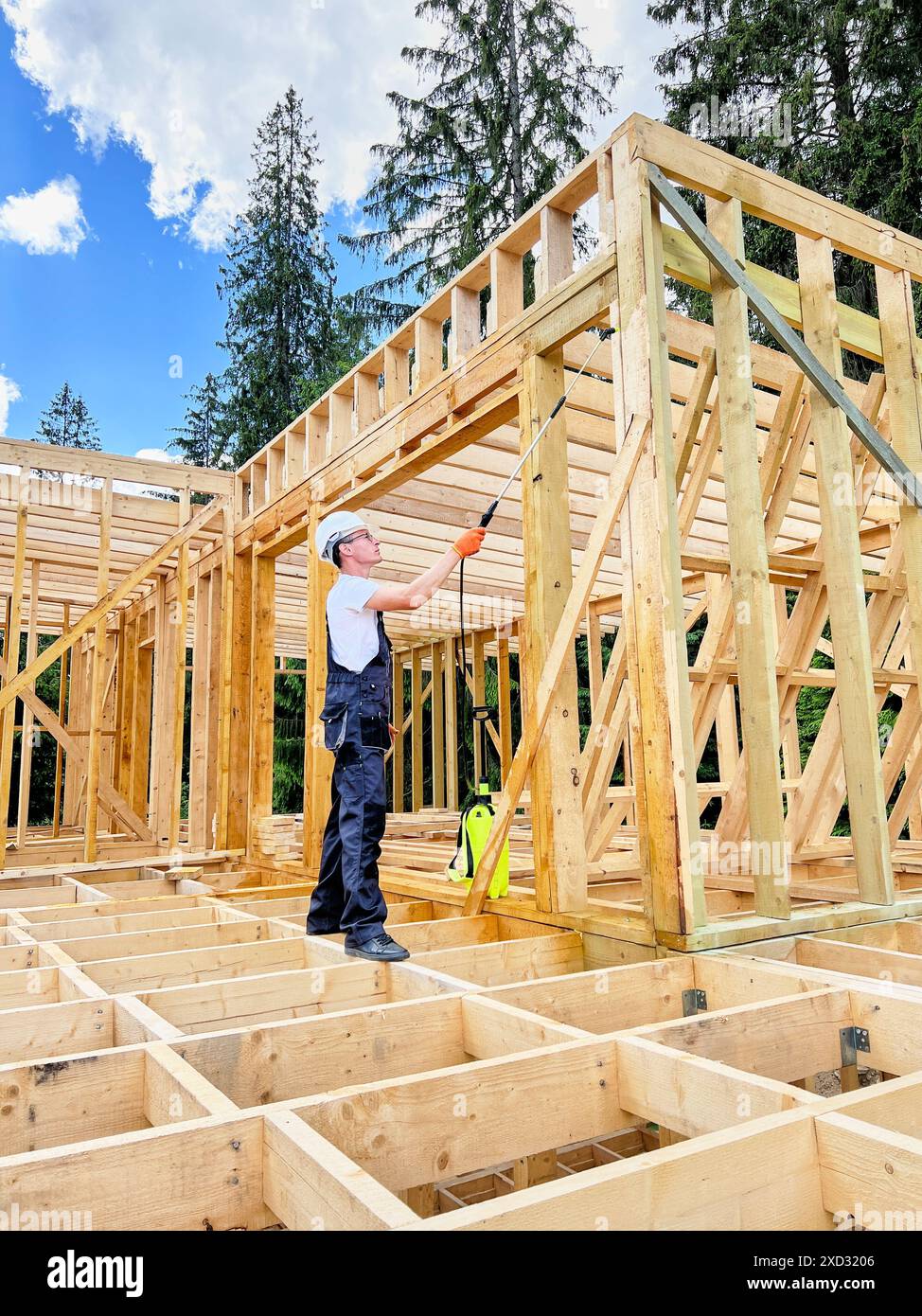 Laborer constructing wooden frame house near forest. Man treating woods, applying fire retardant ...