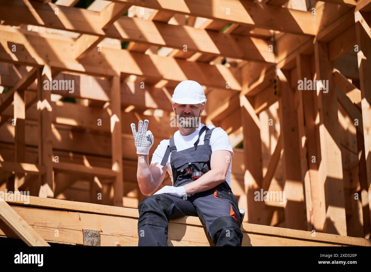 Man manager on construction site of wooden-framed house gestures the OK ...