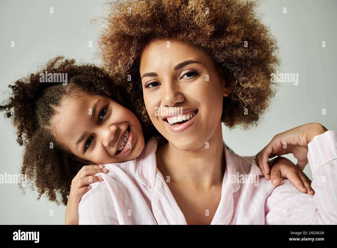 A joyful African American mother and daughter, dressed in pajamas, are ...