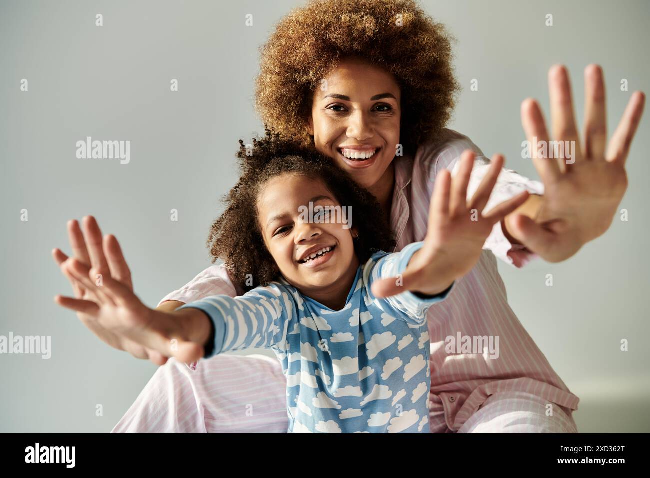 A happy African American mother and daughter in pajamas posing together on a grey background ...