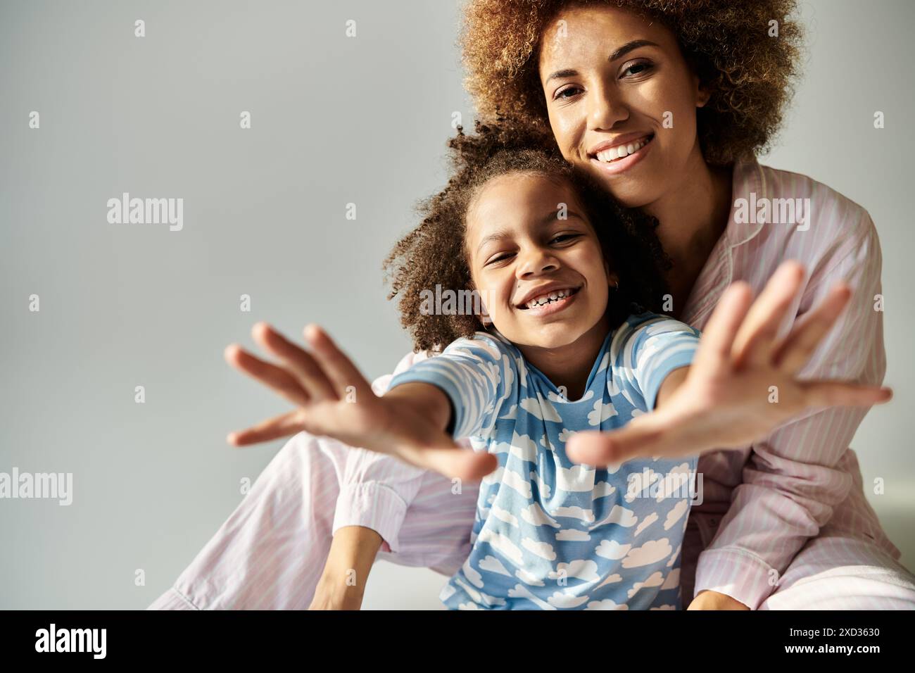 A happy African American mother and daughter in pajamas pose together for the camera against a ...
