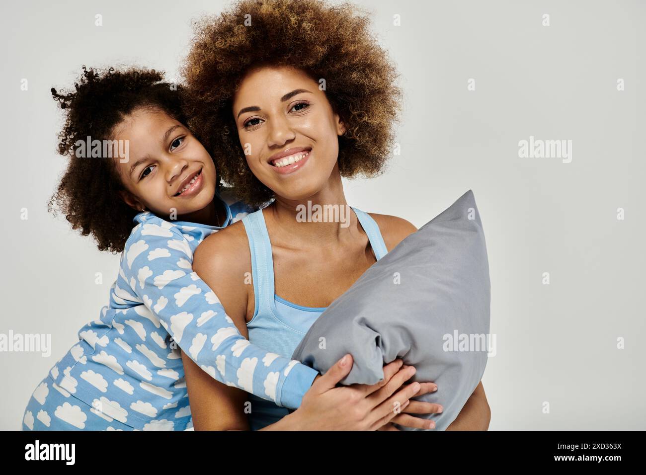 Happy African American mother and daughter in pajamas sharing a loving hug with a pillow on a ...