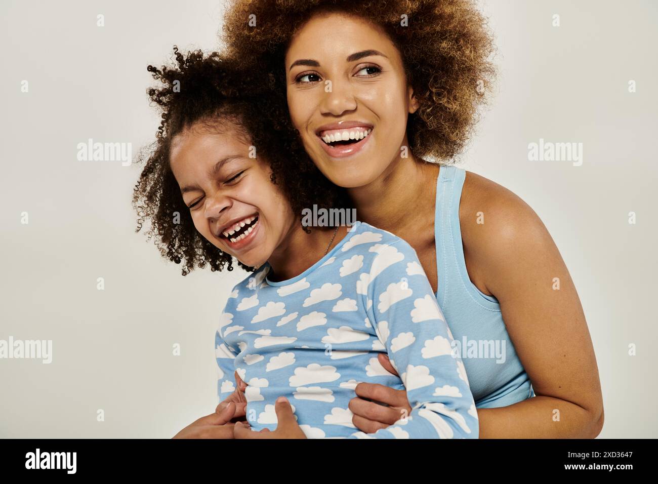 A happy African American mother wearing pajamas hugging her daughter tenderly in front of a ...