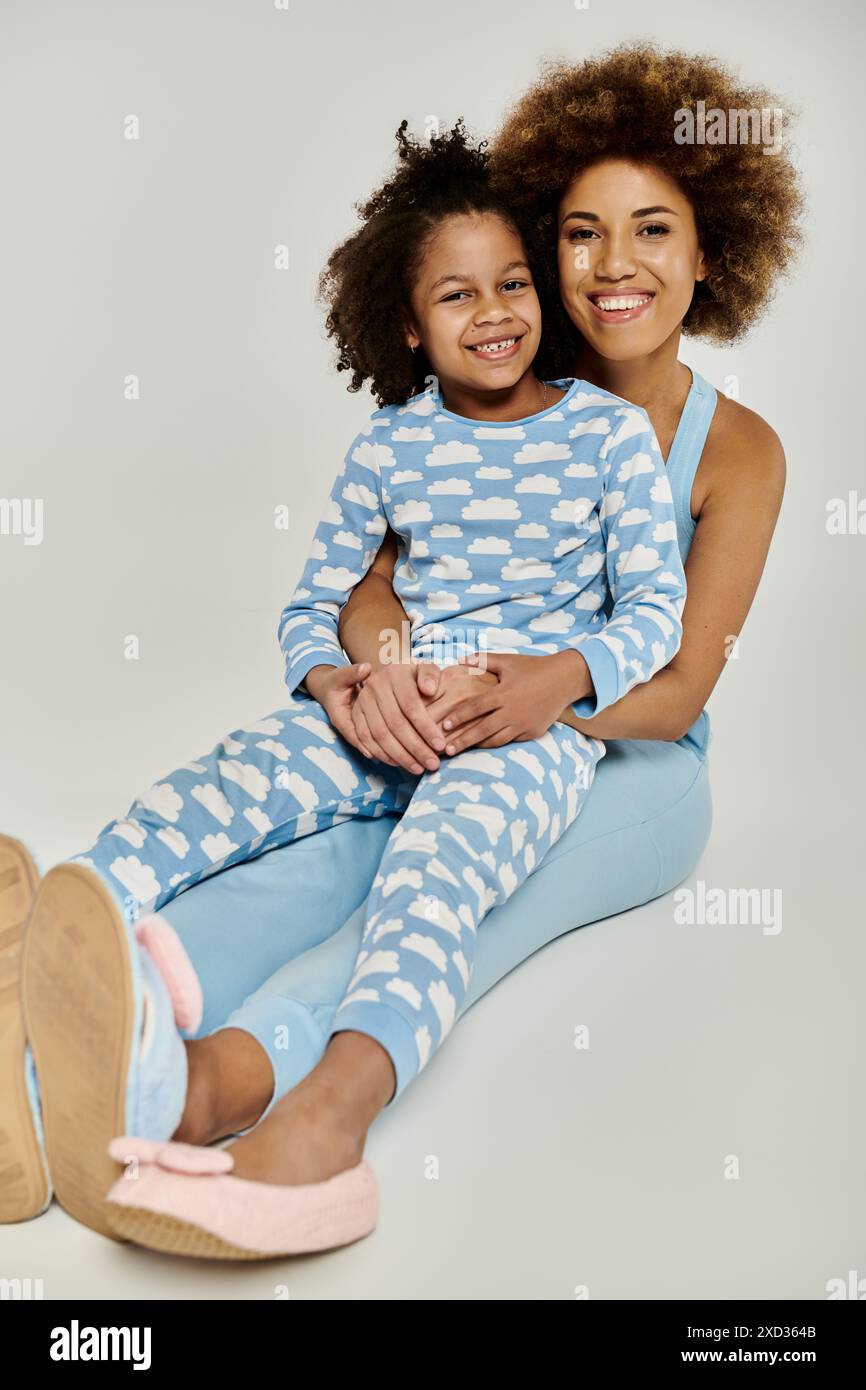Happy African American mother and daughter sitting on the floor in matching blue pajamas ...
