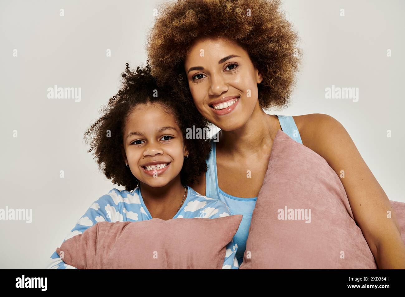 Happy African American mother and daughter smiling in pajamas while posing together on a grey ...