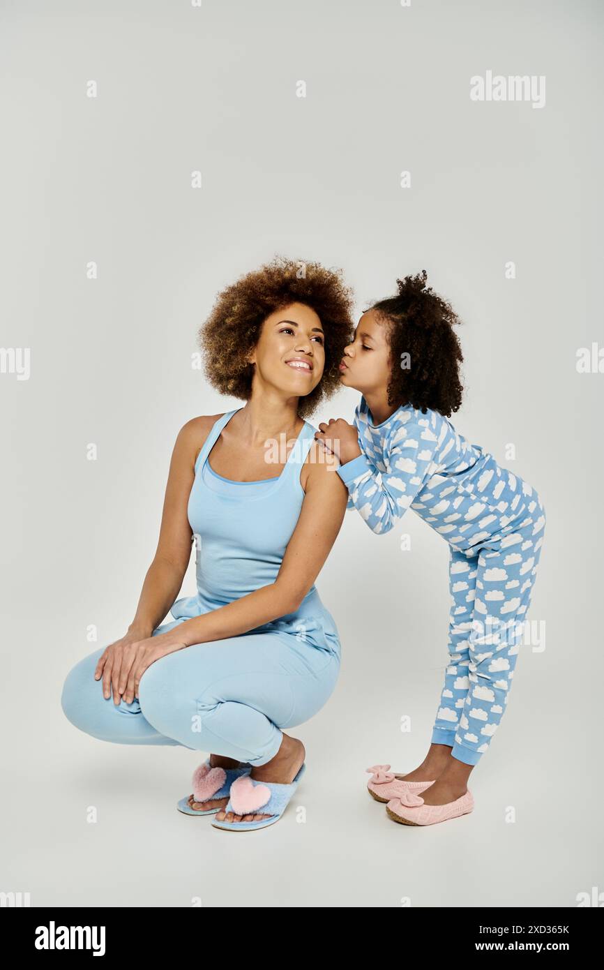 An affectionate moment between a joyful African American mother and daughter, wearing matching ...