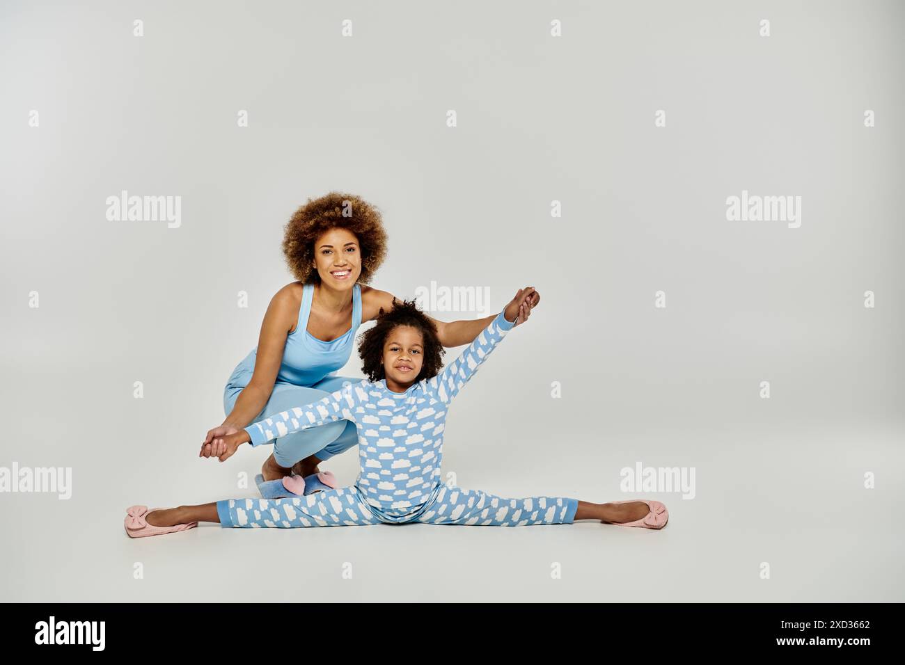 A happy African American mother and daughter in pajamas practicing yoga ...