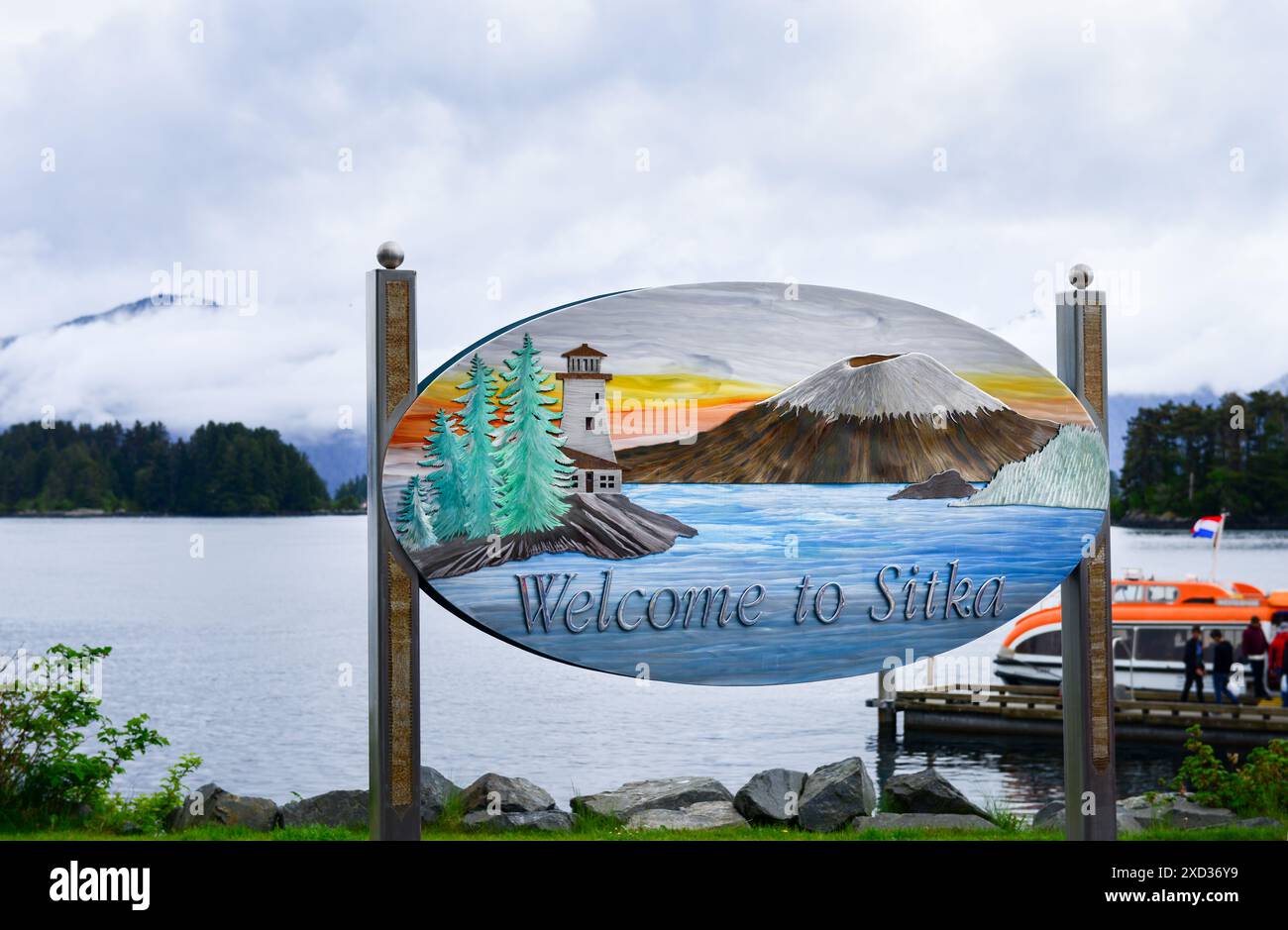 Welcome to Sitka sign on the shore of Sitka. Unrecognizable people from ...